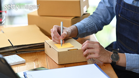 Cropped shot business owner writing address on cardboard box for ...
