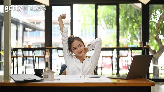Happy young woman relaxing at workplace, reclining back in chair and ...