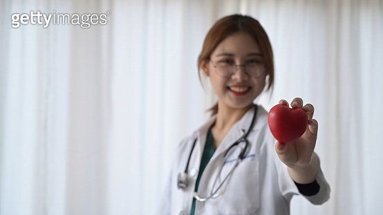 Smiling female doctor in white medical uniform holding red heart shape ...