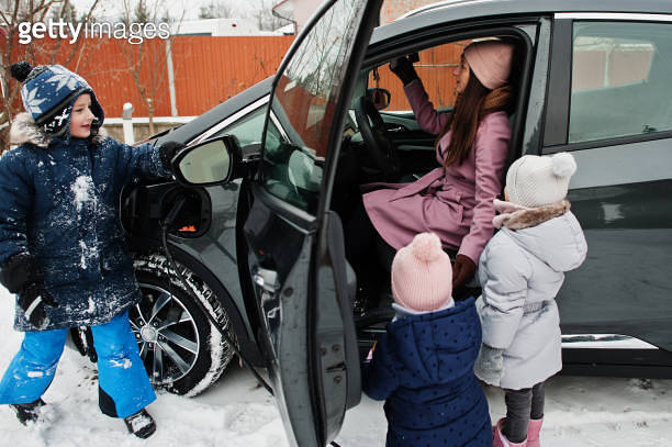 Young mother with kids charging electric car in the yard of her house ...