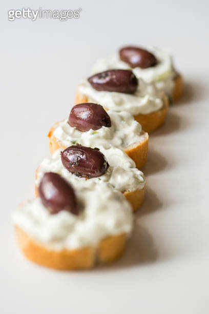 Small piece of bread with tzatziki spread and olive in row on white ...