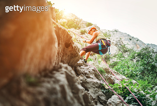 Active climber woman in protective helmet abseiling from cliff rock ...