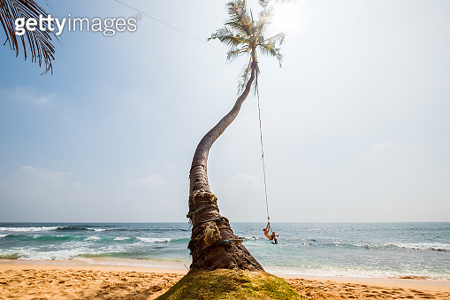 Cheerful teenager boy swinging on palm tree rope on the beach swing ...