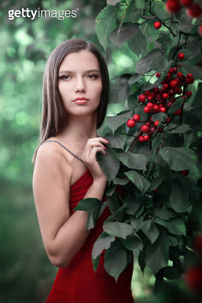 girl in a red dress in a wreath of berries with closed eyes in summer ...