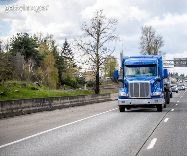 Blue low profile cab big rig semi truck transporting cargo on flat bed ...