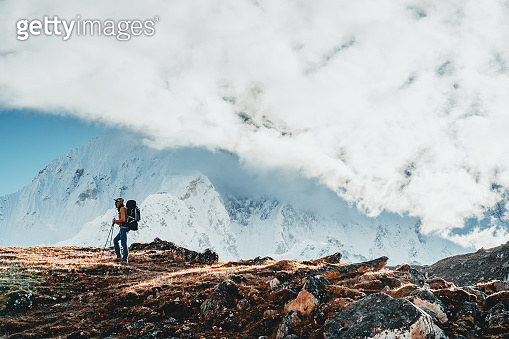 Young tourist walk along high altitude track among snowy and cloudy ...