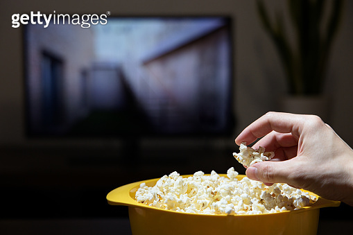 Man's hand grabbing popcorn from a yellow bowl while watching TV ...