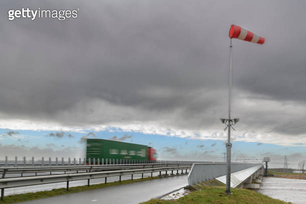 Truck driving over a bridge with a windsock warining sign during a ...