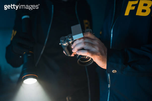 Uniformed FBI agents's hands with a flashlight and a camera with photos ...