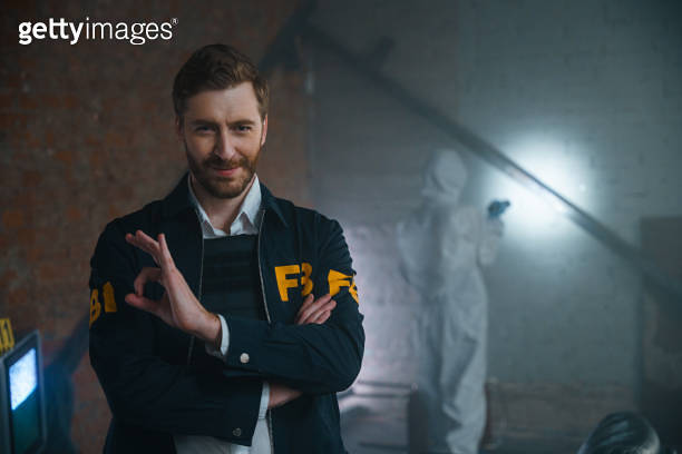 Attractive FBI agent stands with his arms crossed at the crime scene ...