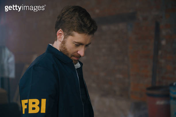 Handsome FBI agent looking down, standing against the brick wall 이미지 ...