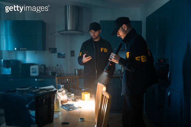 Two FBI agents at the crime scene lighting physical evidences on a table with a flashlight ...