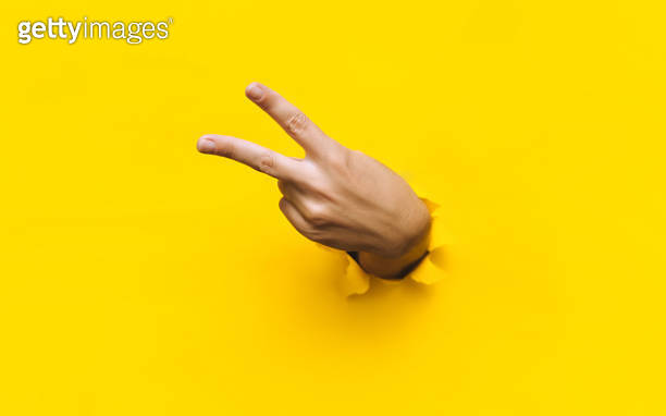 Victory sign two-finger hand gesture on yellow background with torn ...