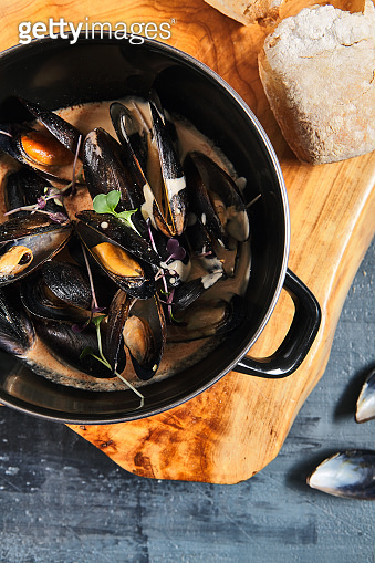 Mussel stew pot with creamy sauce, baguette on stone table. Mussels ...