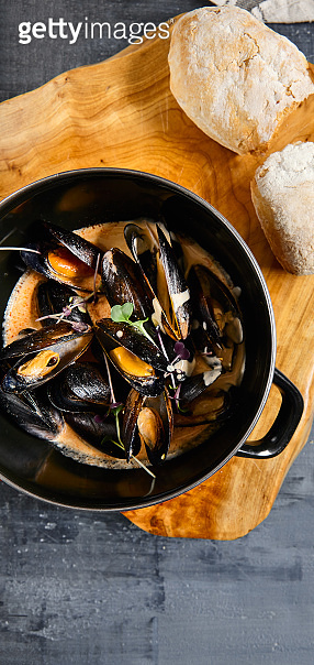 Mussel stew pot with creamy sauce, baguette on stone table. Mussels ...