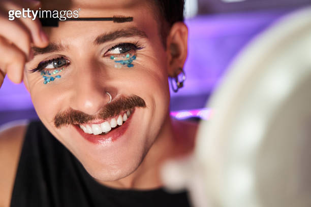Metrosexual man with mustaches holding make up brush near his face and ...
