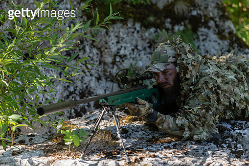 army soldier holding sniper rifle with scope and aiming in forest. war ...