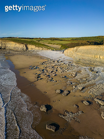 Aerial view of large limestone cliffs and a sandy beach next to the sea ...