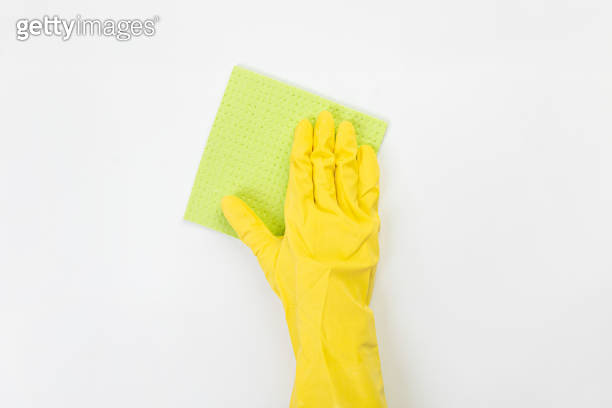 The hand of a housewife in a yellow protective rubber glove holds a ...