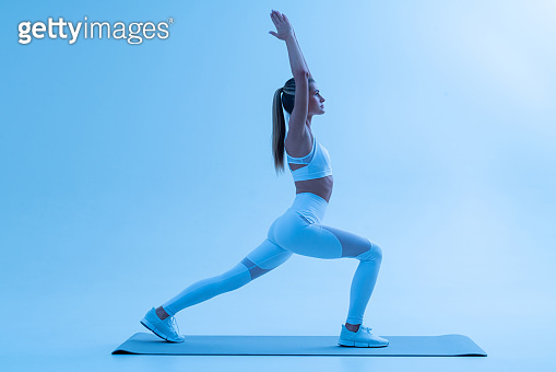 Flexible girl in sportswear standing in warrior pose raising hands ...