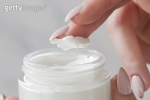 Close up of woman's hand is taking cream from a jar with her finger ...