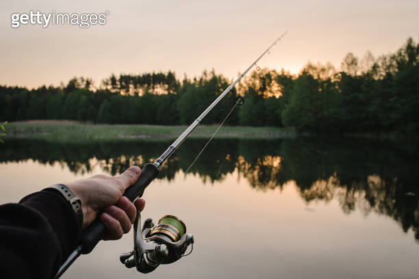 Man catching fish, pulling rod while fishing from lake or pond ...