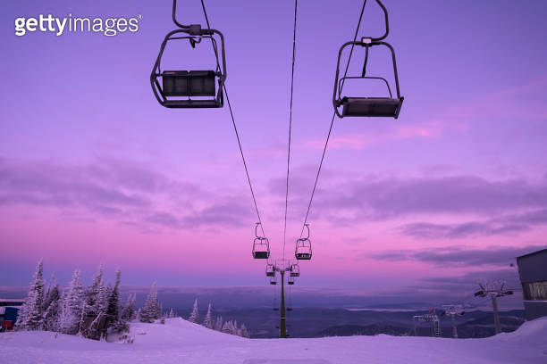 Ski lift in snowfall in mountains ski resort. Pink purple winter sunset ...