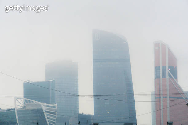 View of the blurry roofs of skyscrapers through the fog. Power line on ...