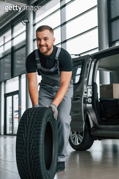 Brand new tire. Man in uniform is working in the autosalon at daytime ...