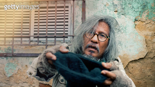 homeless man, dirty dressed, is reaching out for help from passersby ...