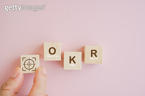 hand holding target icon with OKR dark brown text (Objectives, Key and ...