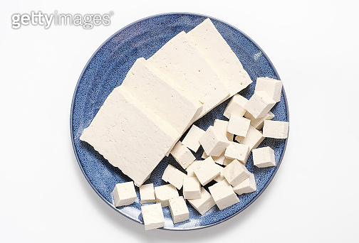 Cut into pieces and cubes of tofu on a blue plate close-up on white ...