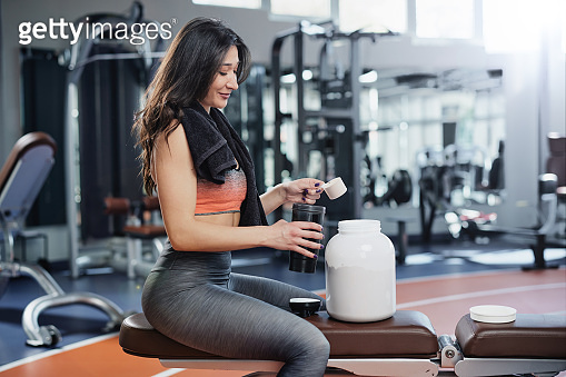 An attractive sportswoman is making a protein shake while sitting on a ...