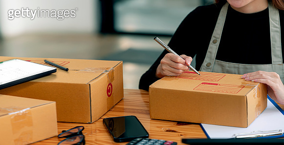 Young woman small business owner writing on parcel box preparing ...
