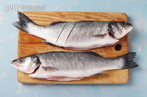 Fresh raw fish seabass on cutting wooden board on blue background ...