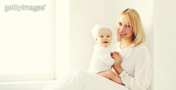 Happy smiling young mom playing with her little baby together in white room at home 이미지 ...