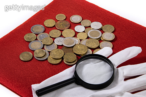Coins with gloves and magnifying glass on red cloth, collection or ...