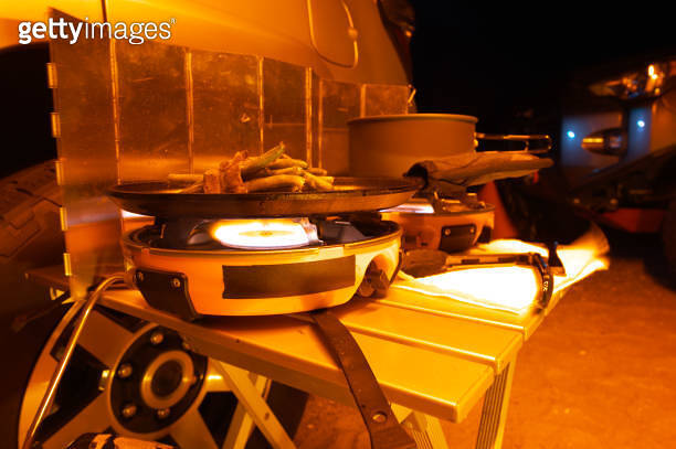 Grilling beans and boiling water in overlanding campsite at night ...