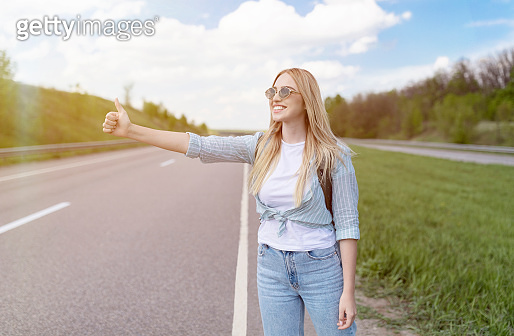 Beautiful young woman in casual wear waving down car, hitchhiking on ...
