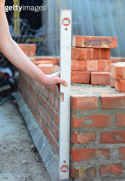 A mason person is using a spirit level to check house brick wall ...