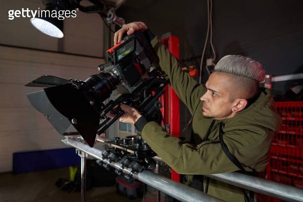 A caucasian videographer tilts a professional movie camera while ...