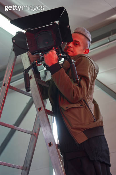 young caucasian man struggles to hold a professional movie camera while ...