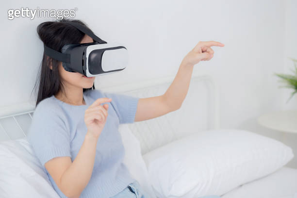 Young asian woman wearing vr headset playing game with excited on bed ...