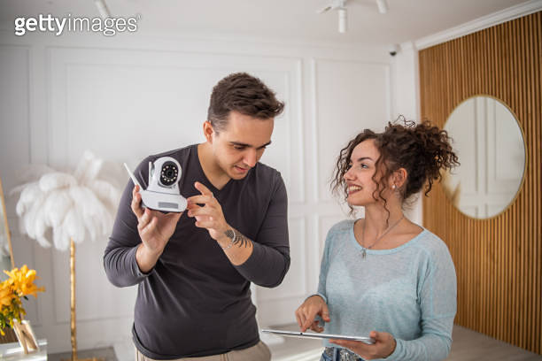 A young couple, a man and a woman, are setting up a security camera for ...