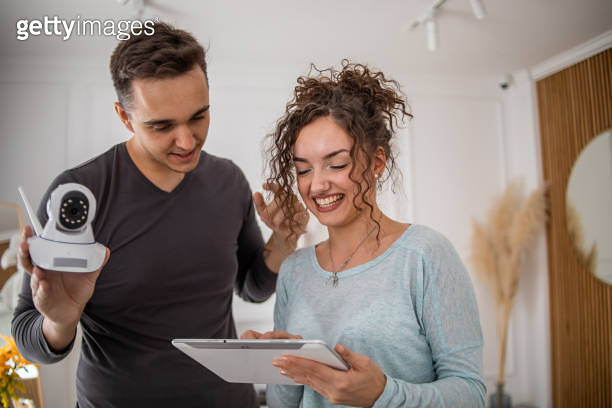 A young couple, a man and a woman, are setting up a security camera for ...