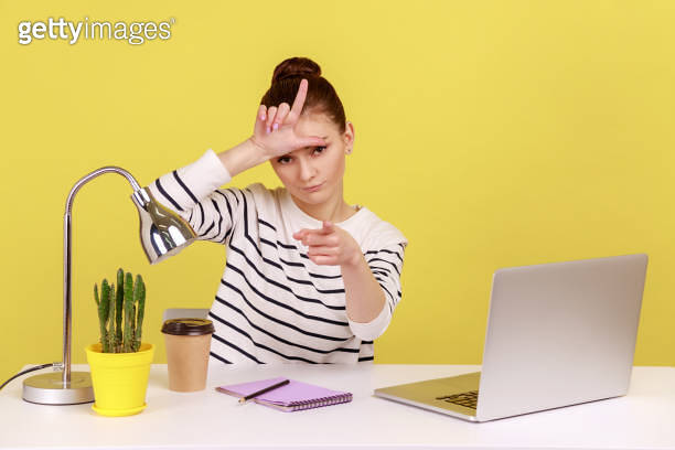 Angry woman sitting at workplace, showing loser gesture, pointing to ...