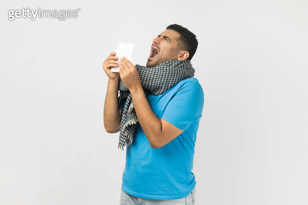 Sick man wrapped in warm scarf standing and sneezing, catching cold in ...