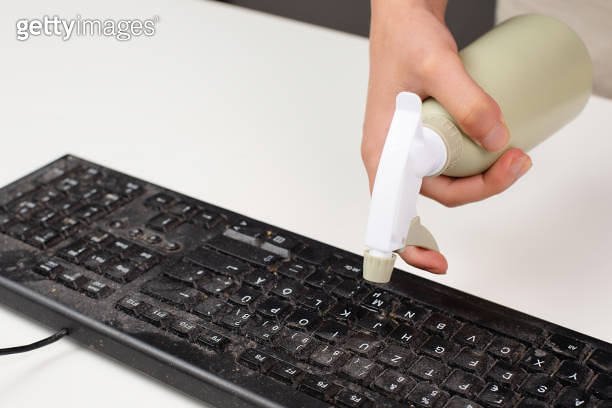 Cleaning computer keyboard in office, spraying water with a spray ...