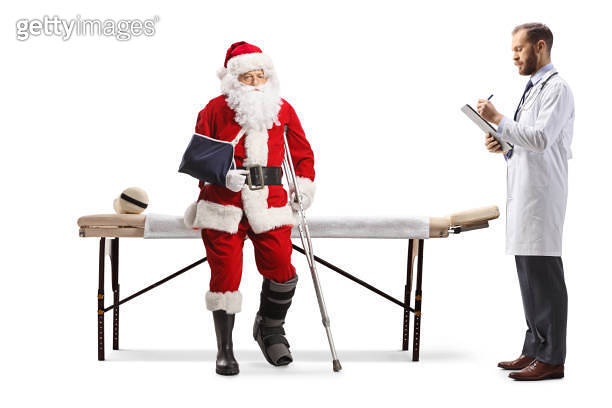 Santa claus with injured leg and arm sitting on a mat table and doctor ...