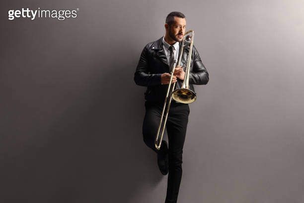 Young man with a trombone standing and leaning on a wall (1458145398 ...